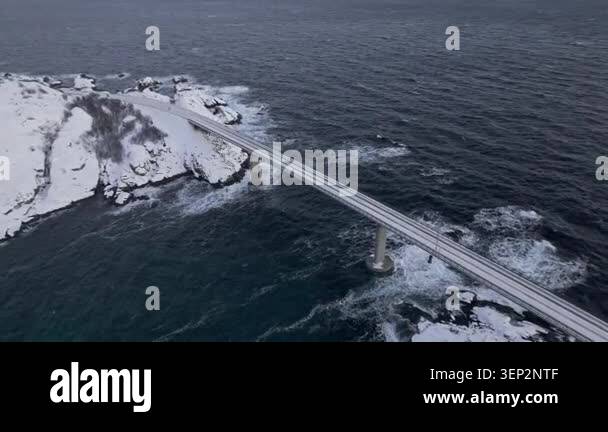 Diagonal elevated bridge crossing dark choppy sea beside a snow-covered ...