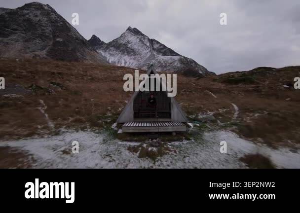 A compact triangular wooden shelter sits centered on a windswept tundra ...