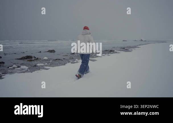 A lone figure in a white puffy jacket, blue pants and a red knit hat ...