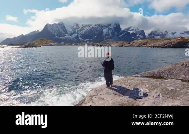 A lone person wearing a dark jacket and red hat stands on wet, rocky ...