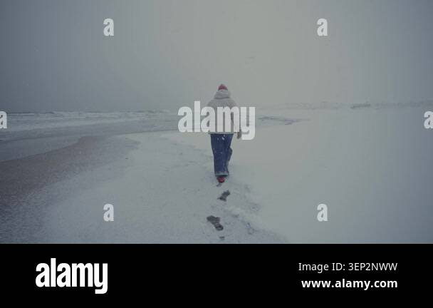 A lone figure in a light puffer jacket, dark pants and knit hat walks ...