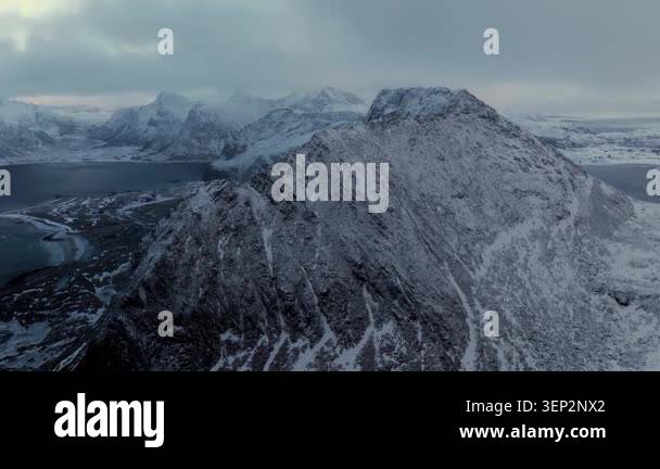 Aerial view of a rugged snow covered mountain peak rising above low ...