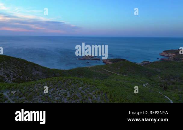 Rolling green hills meeting a calm Mediterranean Sea under a twilight ...