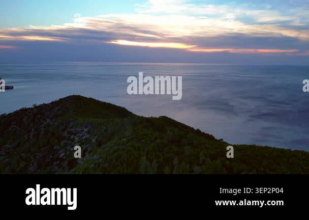 Rolling green hills meeting a calm Mediterranean Sea under a twilight ...