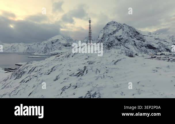 A metal communications tower stands on a windswept snowy ridge ...