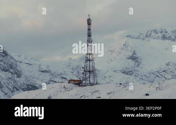 Tall metal radio tower rises beside a small wooden utility hut on a ...