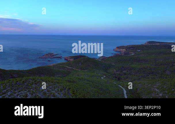 Rolling green hills meeting a calm Mediterranean Sea under a twilight ...