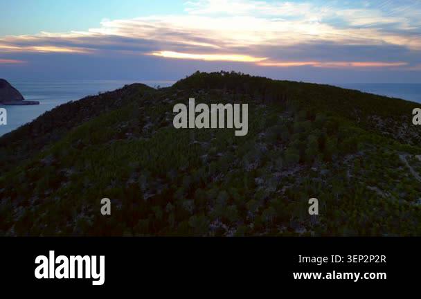 Rolling green hills meeting a calm Mediterranean Sea under a twilight ...