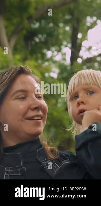 Mother holding white toddler close under green canopy, closeup portrait ...