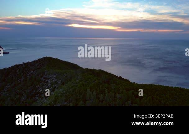 Rolling green hills meeting a calm Mediterranean Sea under a twilight ...