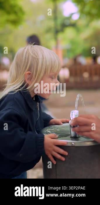 Toddler enjoying fountain sip amid busy park path caregivers guiding ...