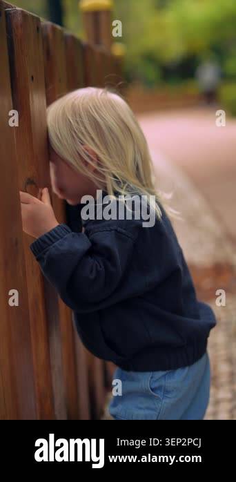Blonde toddler playing hide and seek around wooden railing peeking ...