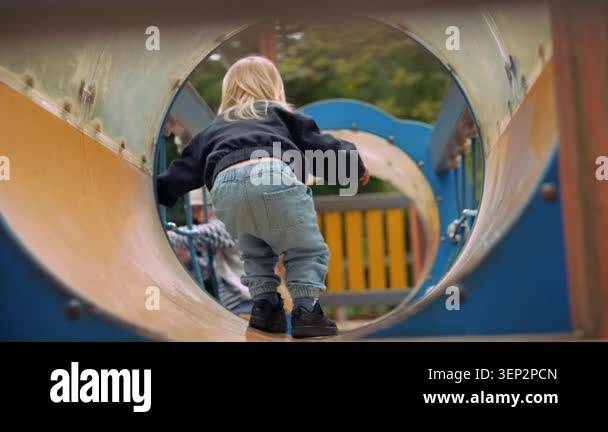 White toddler balancing through playground tunnel, reaching forward ...