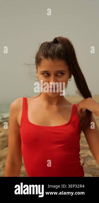 Smiling woman posing by rocky shore, red top laughter and playful ...