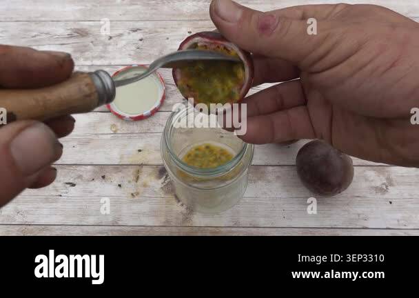 Man extracting fresh passion fruit seeds with a spoon into a glass jar ...