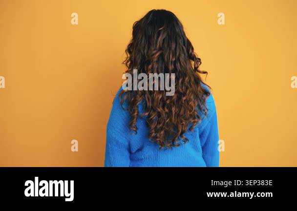 Joyful young woman with long dark curly hair standing with her back to ...