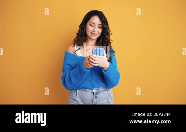 Cheerful young woman with curly hair happily texting and browsing on ...