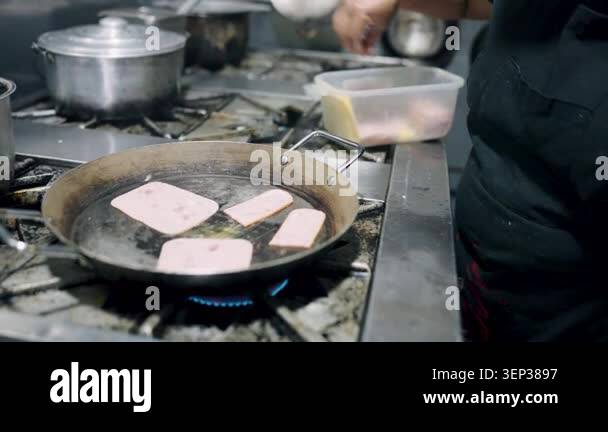 Professional cook placing slices of ham in a hot pan over a gas flame ...