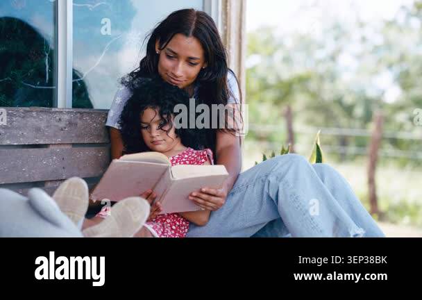 Loving Latina mother teaching her daughter how to read a book. They are ...