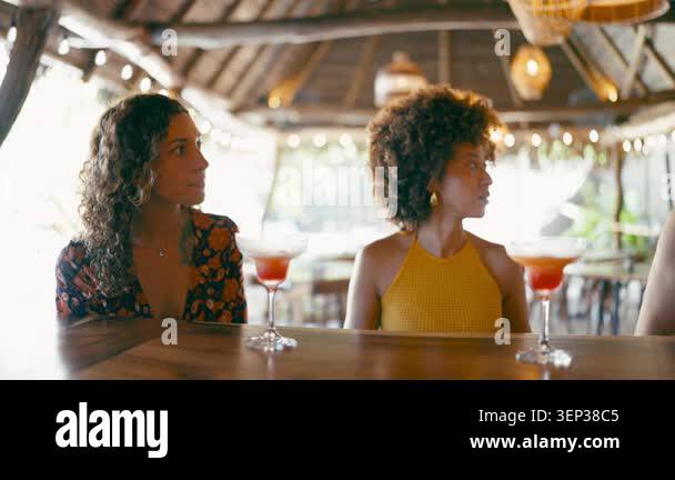 Two beautiful diverse female friends sitting at a wooden bar counter ...
