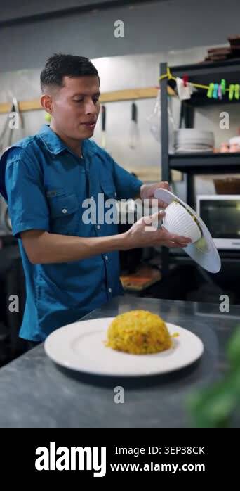 Male cook carefully plating a side dish of yellow rice with vegetables ...