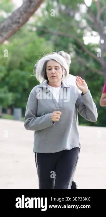 Healthy mature woman with gray hair jogging and smiling in a park ...