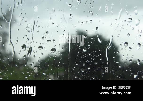Rainwater drops falling on a glass window during a storm with a blurry ...