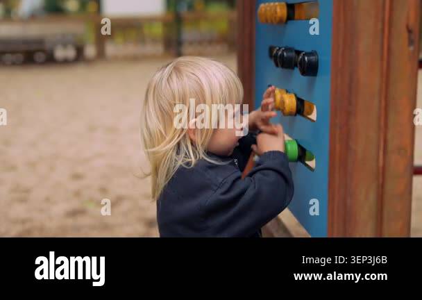 Blond white toddler touches activity panel, wooden knobs, focused ...