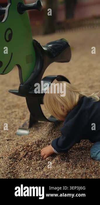 White toddler exploring pebbles under green rocker, blonde child ...