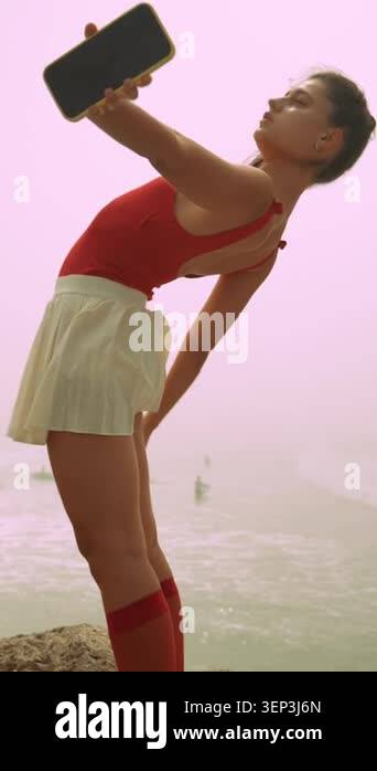 Young woman offering smartphone toward camera on cliff edge, red top ...