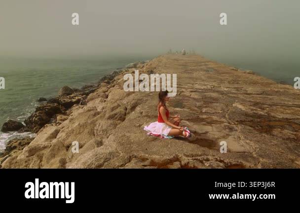 Young woman watching ocean from jetty, soft fog, contemplative pose ...