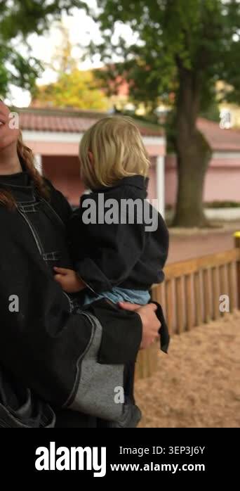 Mother holding toddler outdoors laughing warmly, denim bag and black ...
