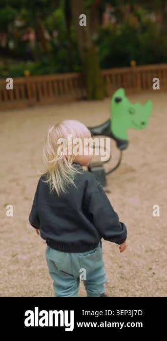 Blonde caucasian toddler attempting mount on green spring rocker ...