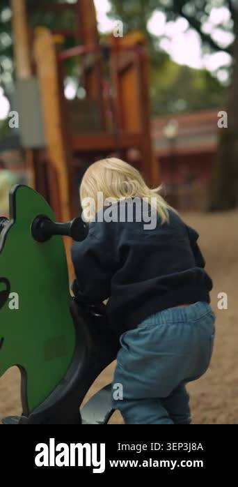 White toddler perched on green rhino watching playground tower, blonde ...