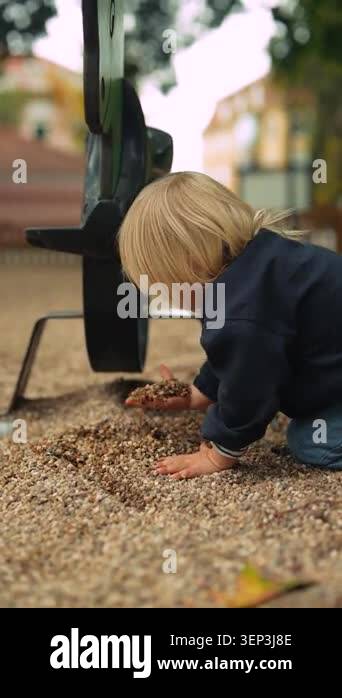 White toddler climbing green rocker, testing balance on gravel, blonde ...