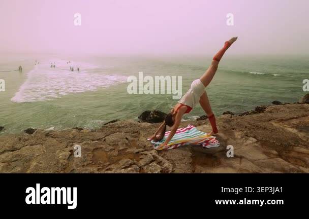 Young woman executing handstand on cliff towel, expansive ocean ...