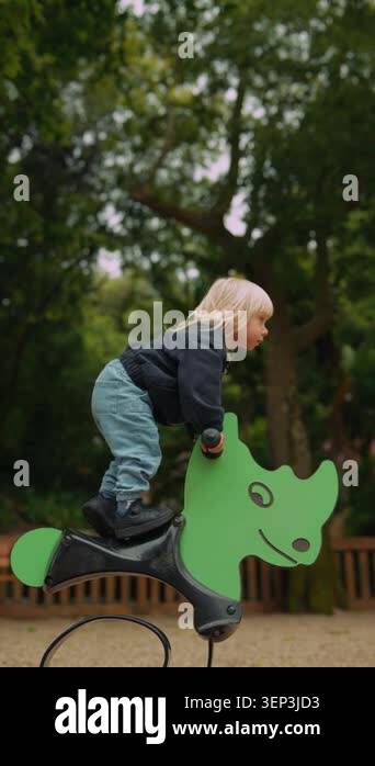 White toddler riding green rhino rocker in leafy park, blonde child ...
