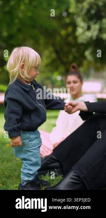 Blonde toddler in park taking tentative steps caregiver offering hand ...