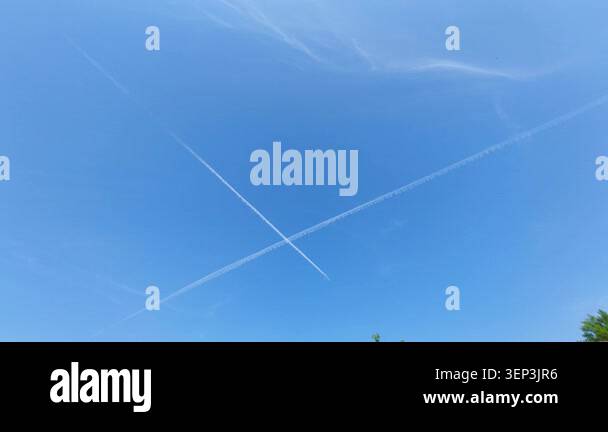 Two airplane contrails crossing in the blue sky forming an X shape ...