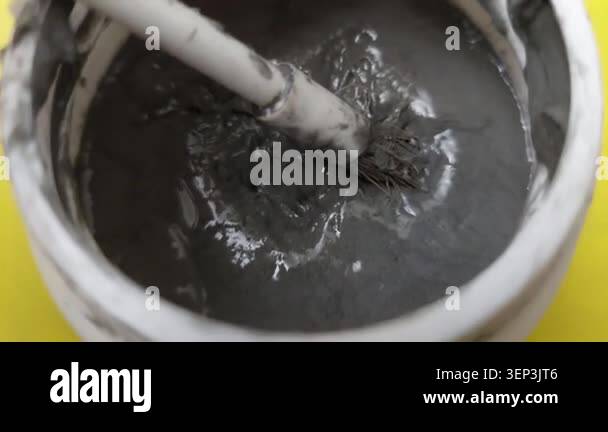 Top down close-up of a small paint brush stirring a thick grey liquid ...