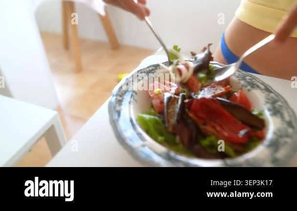 Close view of hands preparing a fresh salad with spoons in a pink bowl ...