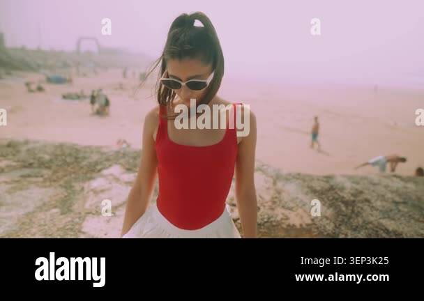 Woman red swimsuit rock overlook beach, sunglasses downcast, hands in ...