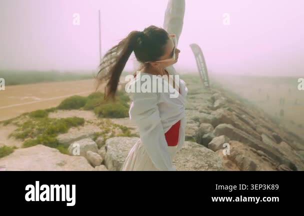 Young white woman celebrating on cliff with arms raised, ponytail and ...