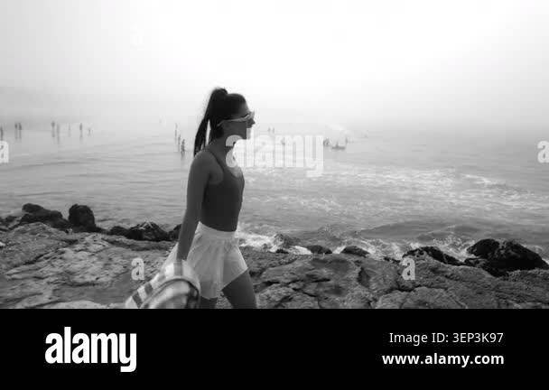 Woman walking along rocky coastline in black and white, minimalist ...