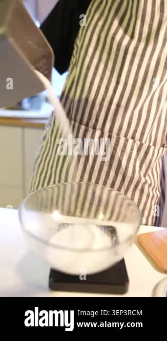 Young woman pouring sugar into bowl on digital scale striped apron ...
