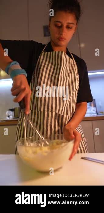 Closeup woman whisking thick batter, striped apron, vigorous strokes ...