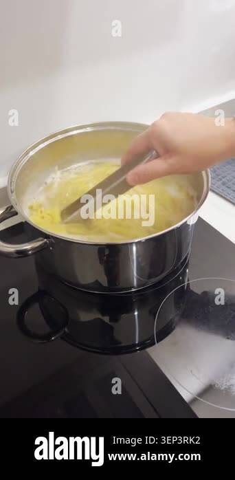 Hand stirring boiling pasta in stainless steel pot on kitchen stove ...