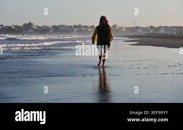 A person walking barefoot along the wet sand at the edge of the ocean ...