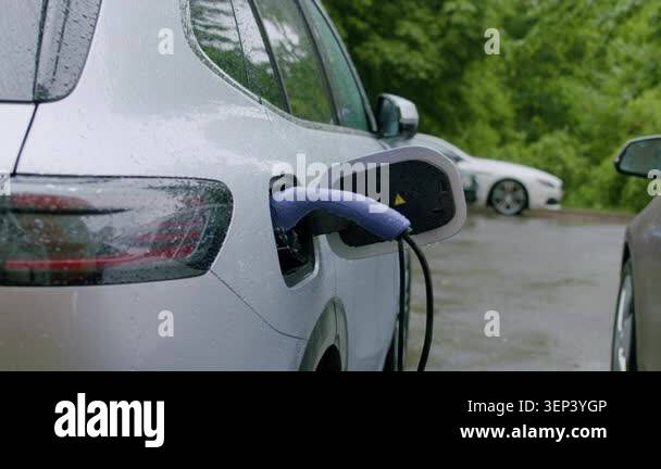 Electric vehicle is charging in the rain, with a charging cable ...