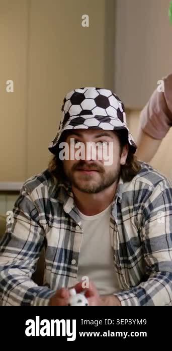 Male in a soccer-patterned bucket hat engages with a video game ...